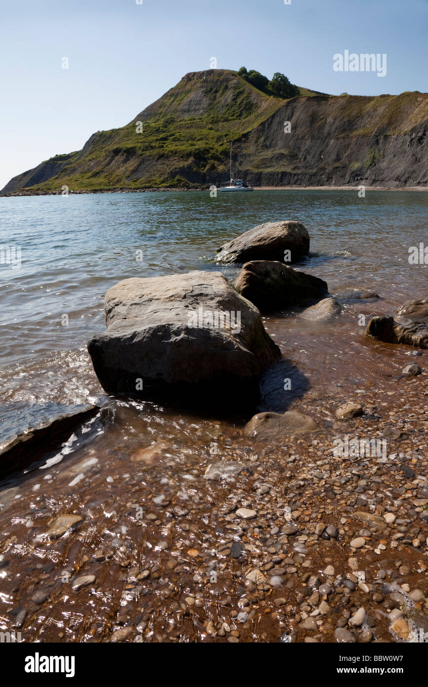 Rocks on beach and rugged landscape in distance on warm summer's day ...