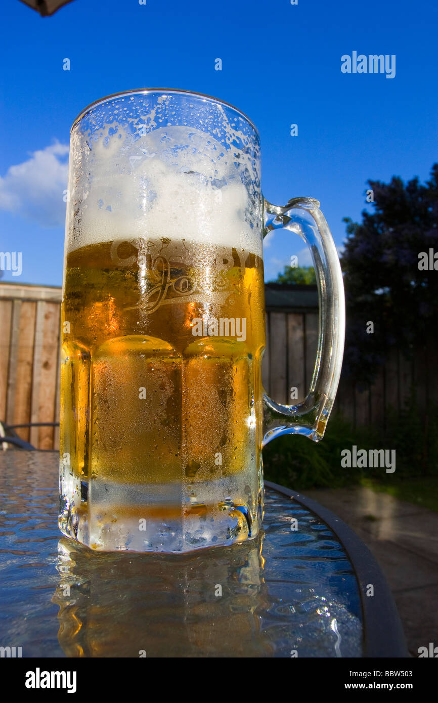 Cold beer in glass with frothy head in sunshine atop a patio table ...