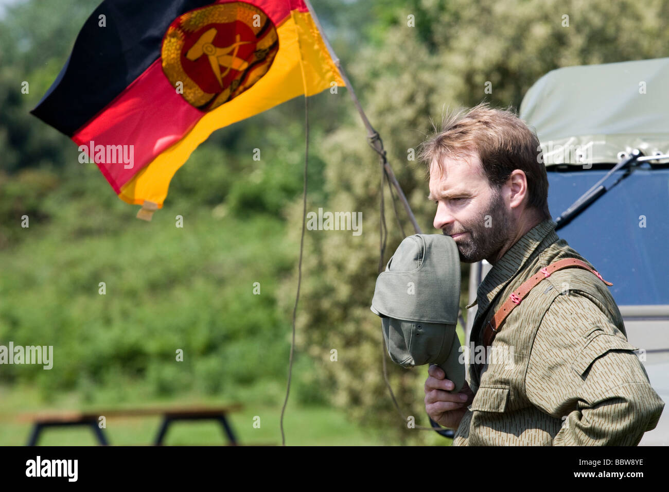 Man in East German army uniform looks thoughtful in front of an East ...