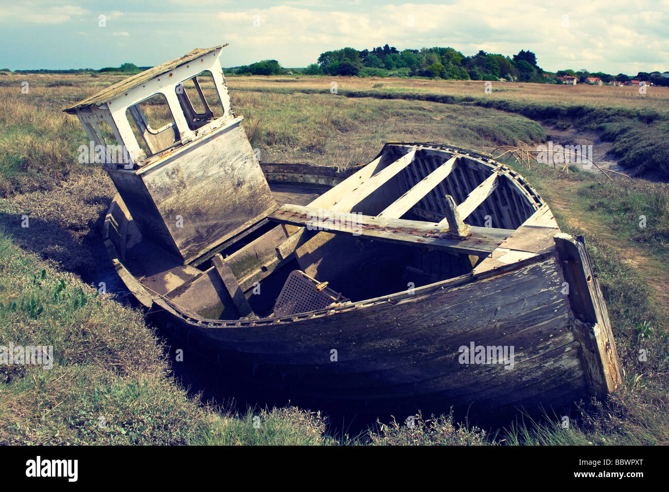 A wrecked fishing boat lying on its side in mud on the marshes of the ...