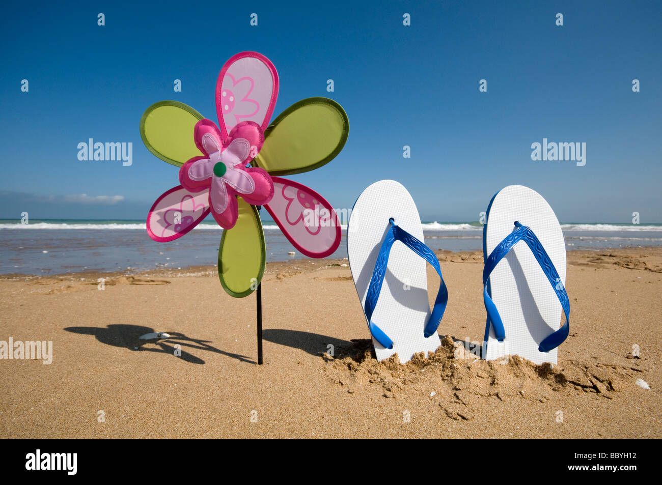 Flip flops and windmill in sand on beach Stock Photo - Alamy