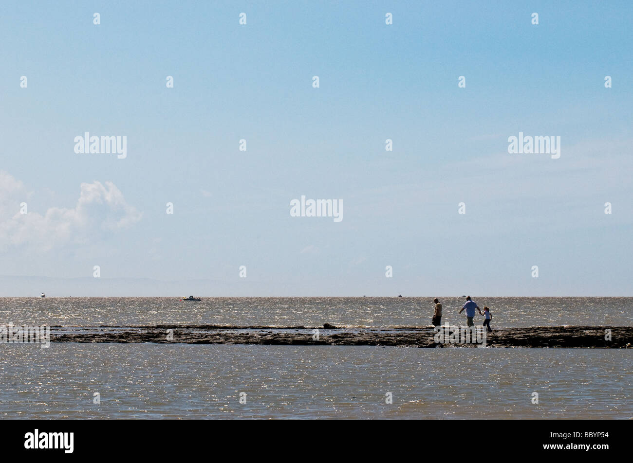 Three people walking across the causeway to Sully Island in South Wales ...