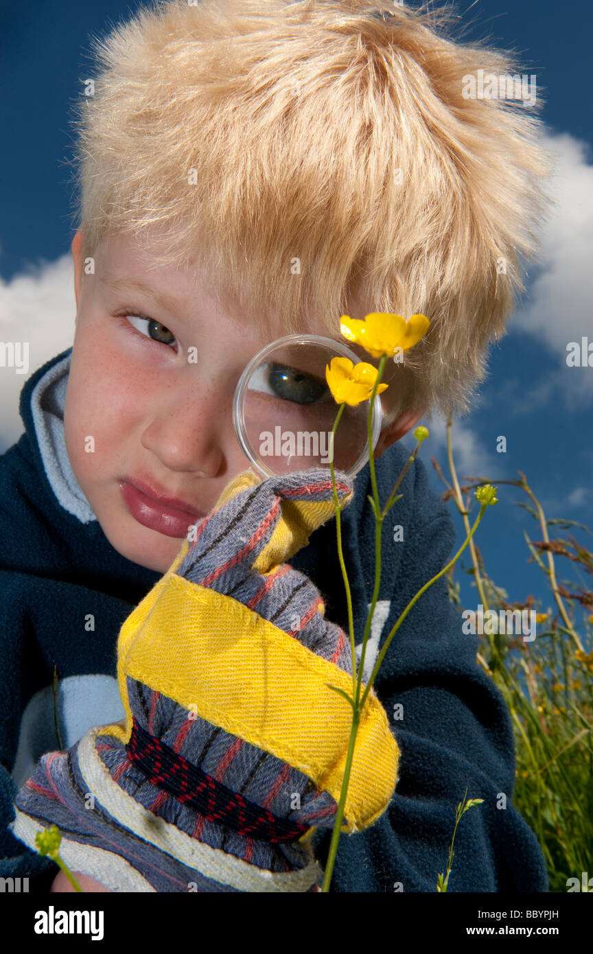Young boy with magnifying glass looking at flowers and bugs in ...