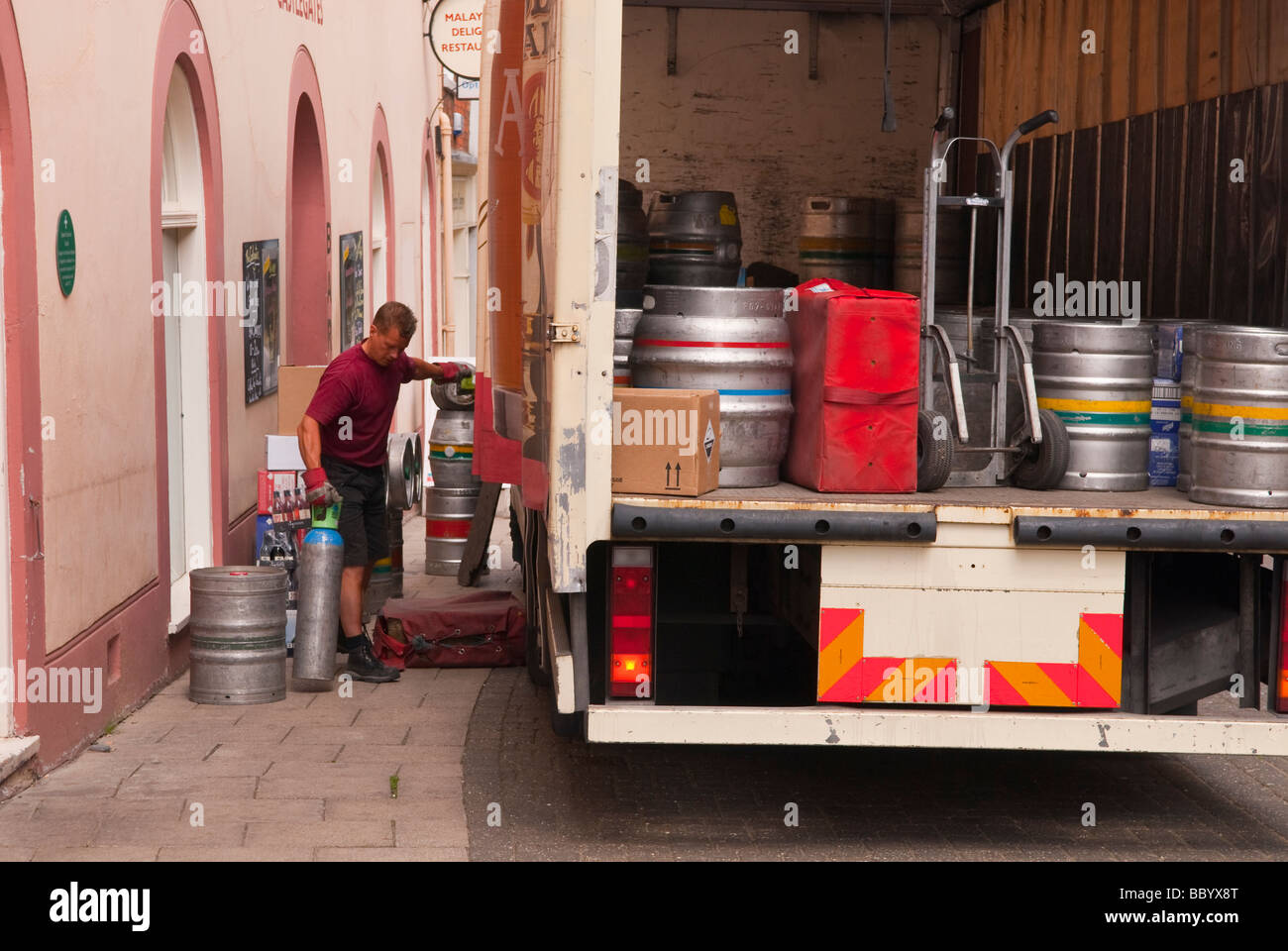 A male man worker unloading beer barrels from the back of a lorry in a ...