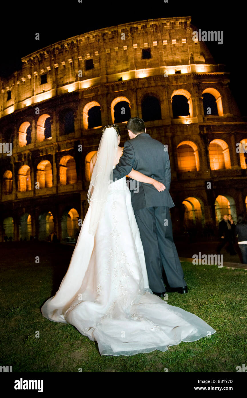 Rear view of bride and groom standing outside the Coliseum at night ...