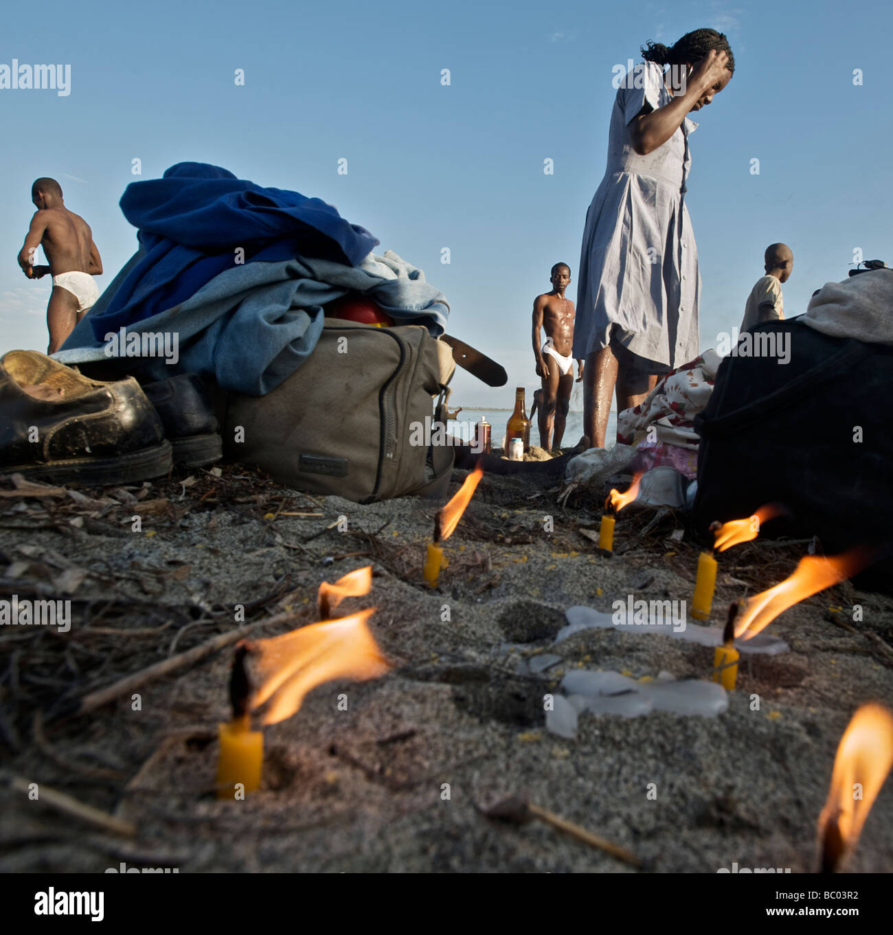 Voodoo worshipers stand on the beach in front of candles stuck in the ...