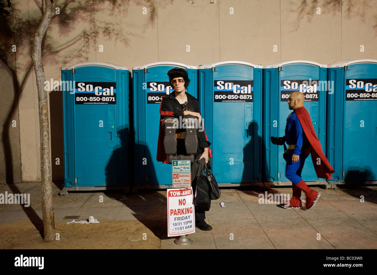 Two men dressed as Elvis and Superman stand near outhouses during the ...