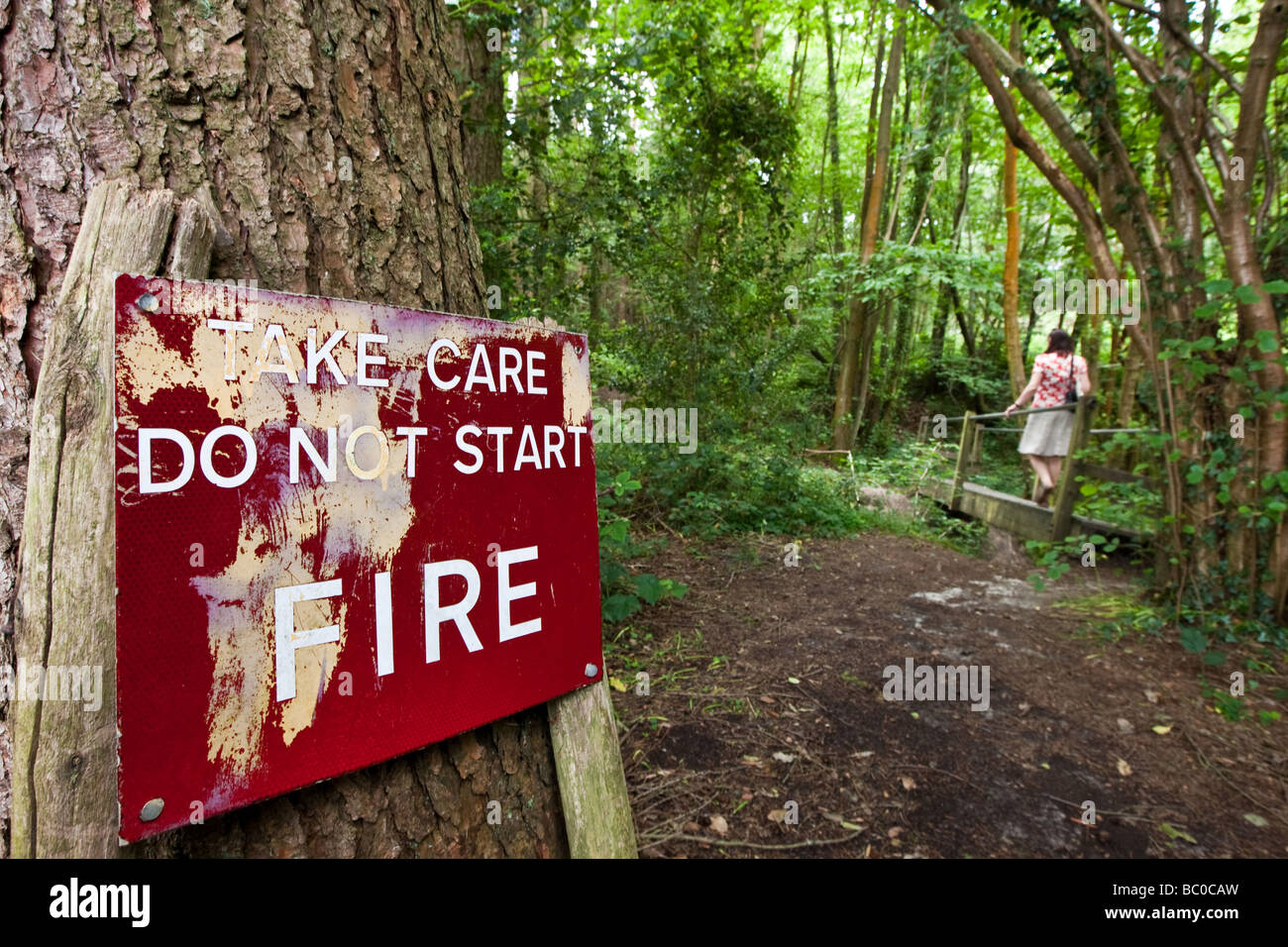 Woman walks past a sign that says Take Care Do Not Start Fire on a ...