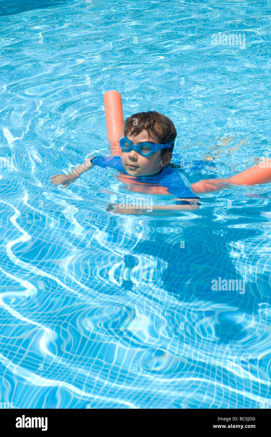 Boy aged 6 swims with the aid of a woggle or noodle in a pool in ...