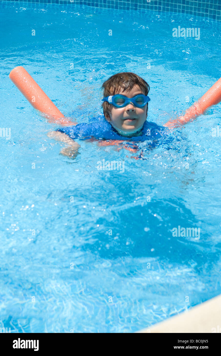Boy aged 6 swims with the aid of a woggle or noodle in a pool in ...