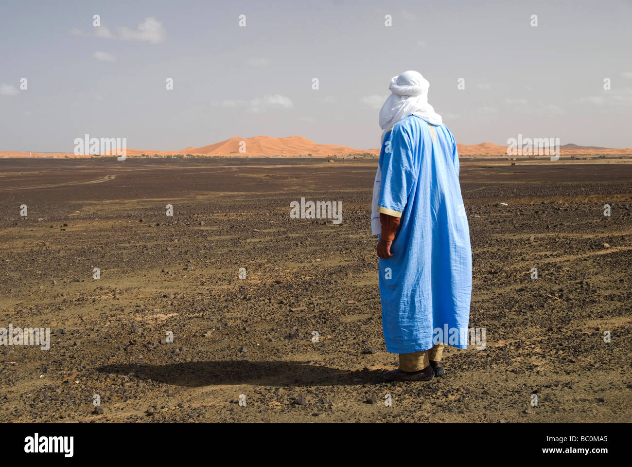 A Berber man in traditional dress leads stands in the Sahara desert ...
