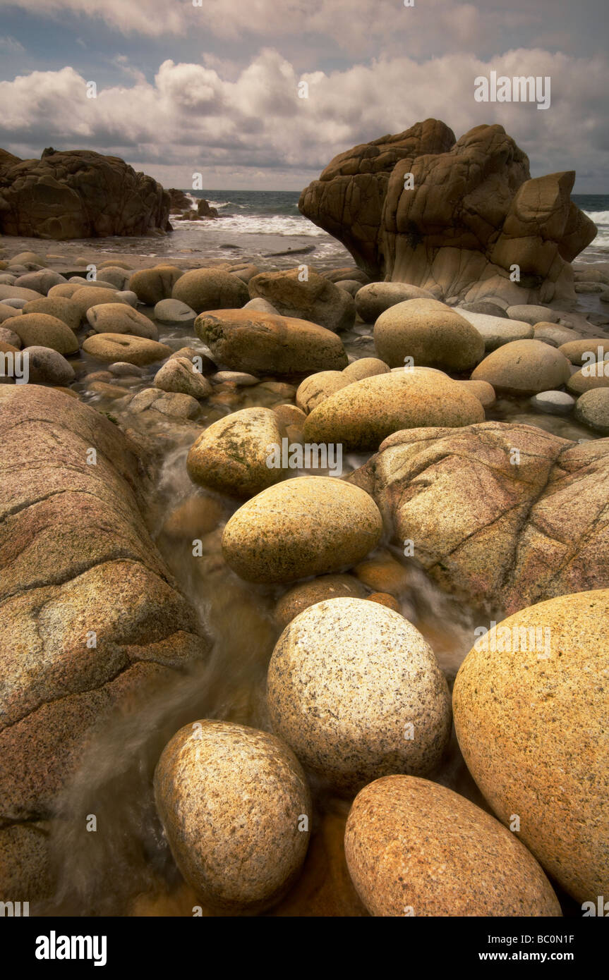 Waves rushing in around large round boulders on the beach at Porth ...