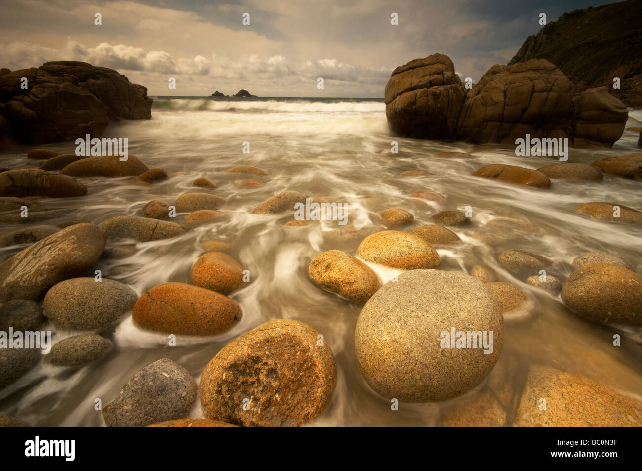 Waves rushing in around large round boulders on the beach at Porth ...
