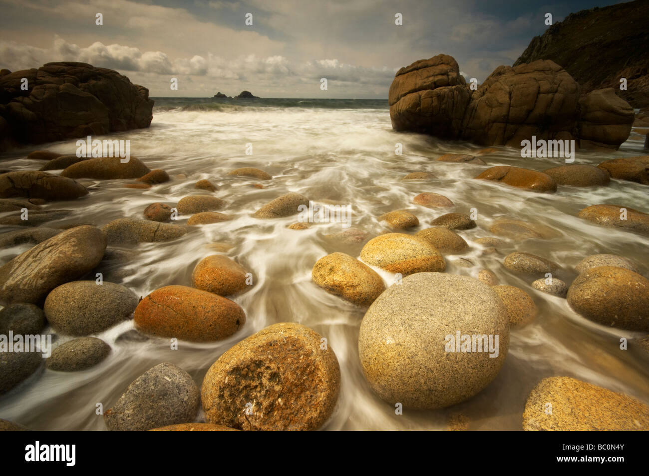 Waves rushing in around large round boulders on the beach at Porth ...