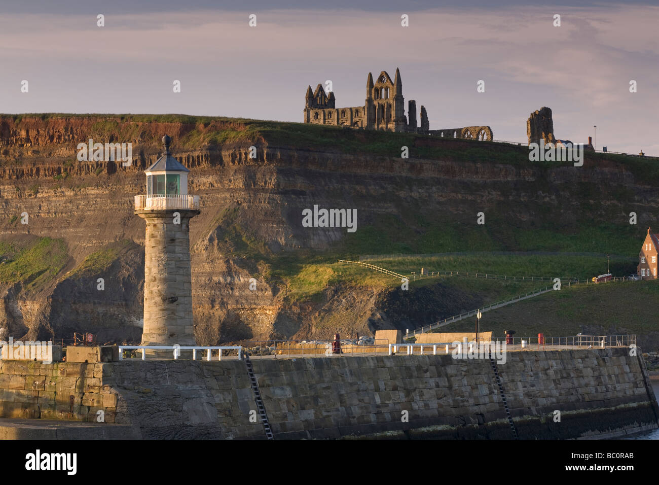 The lighthouse on Whitby Pier with St. Hilda's Abbey on the cliffs in ...