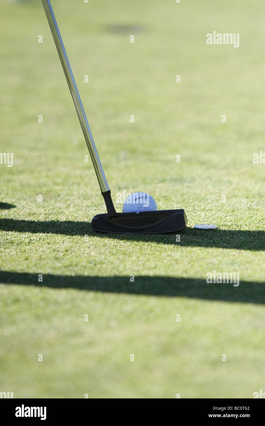 A close-up of a putter set up behind a golf ball on a golf green, with ...