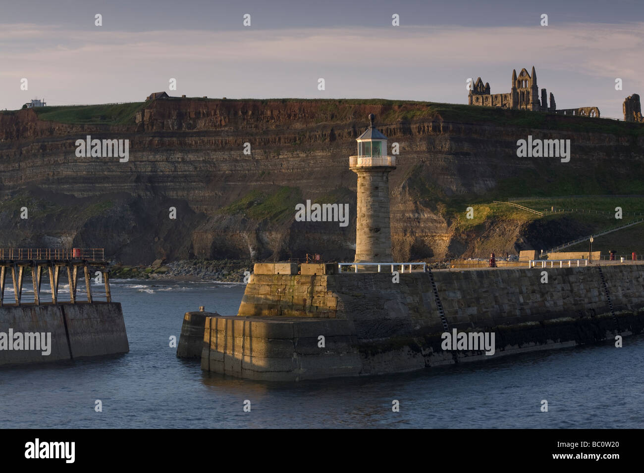 The lighthouse on Whitby Pier with St. Hilda's Abbey on the cliffs in ...