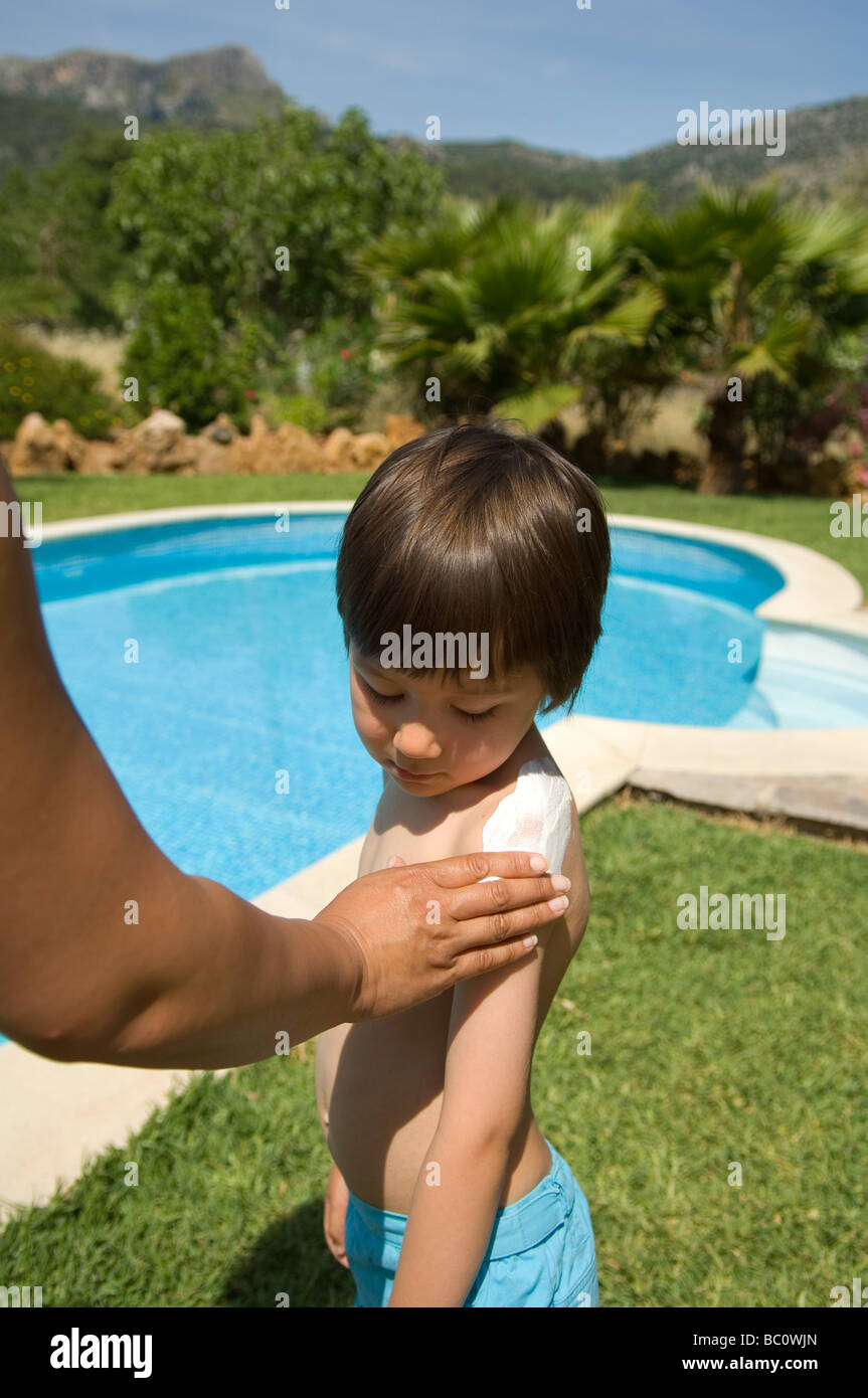 Boy aged six years has suncream applied to shoulder before playing in ...
