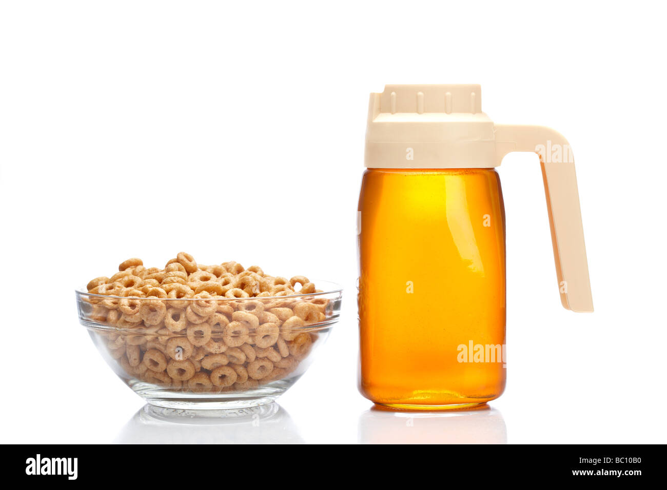 Honey pitcher and glass bowl of cornflakes reflected on white ...
