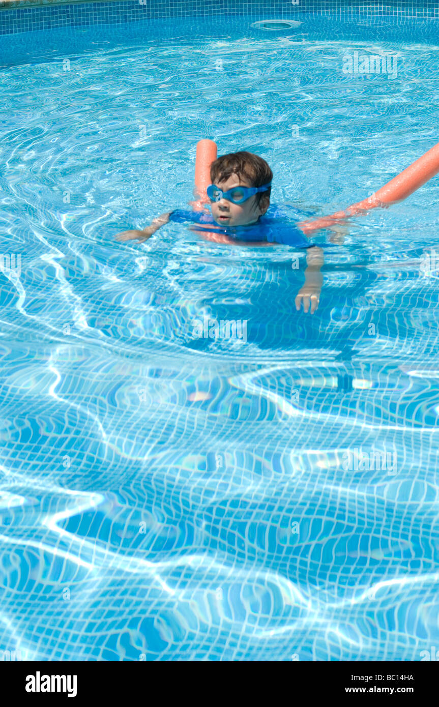 Boy aged 6 swims with the aid of a woggle or noodle in a pool in ...