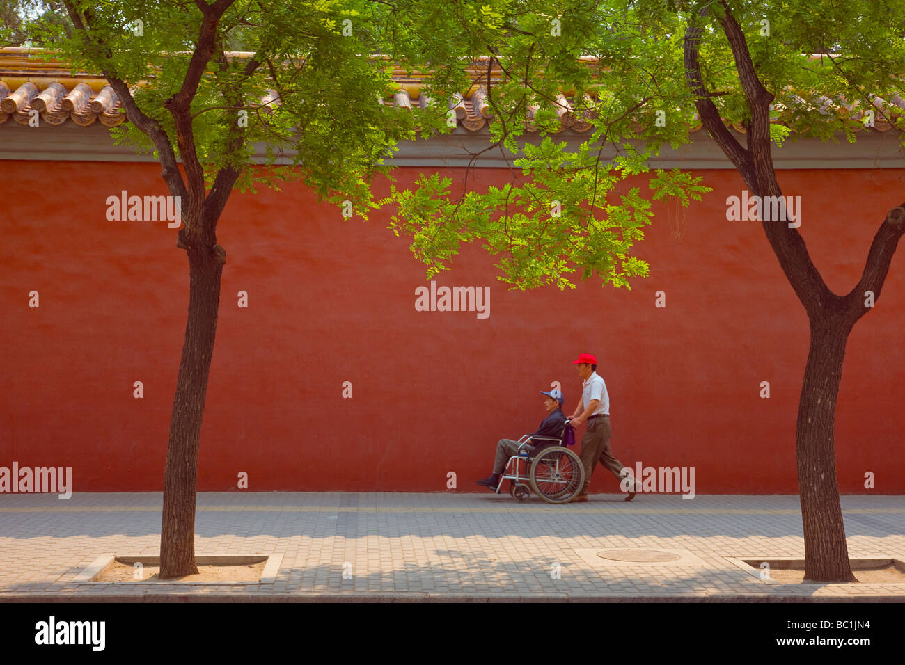 Man pushing wheelchair with ancient red wall of the Forbidden City ...