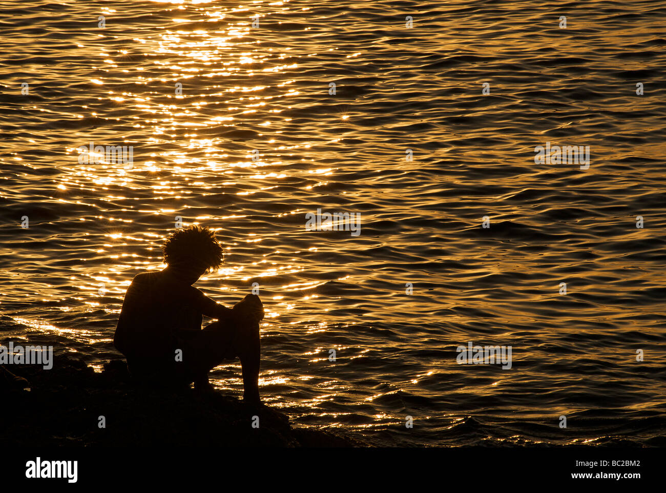 Silhouette of young Cuban man sitting on the rocks by the Malecon ...