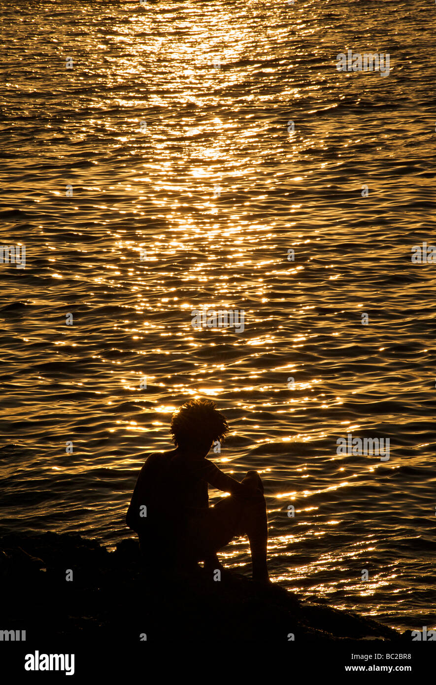 Silhouette of young Cuban man sitting on the rocks by the Malecon ...