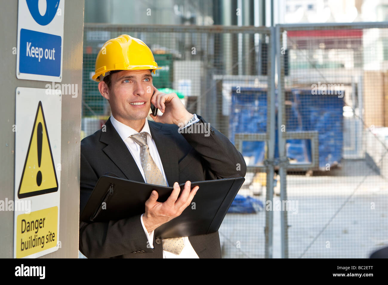 A male manager on a construction site wearing a hard hat and talking on ...
