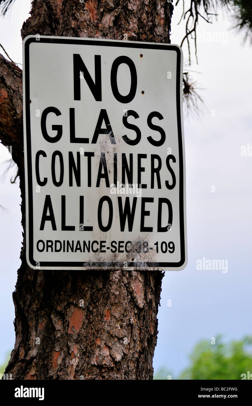 A sign nailed to a tree says No Glass Containers Allowed near a lake in ...