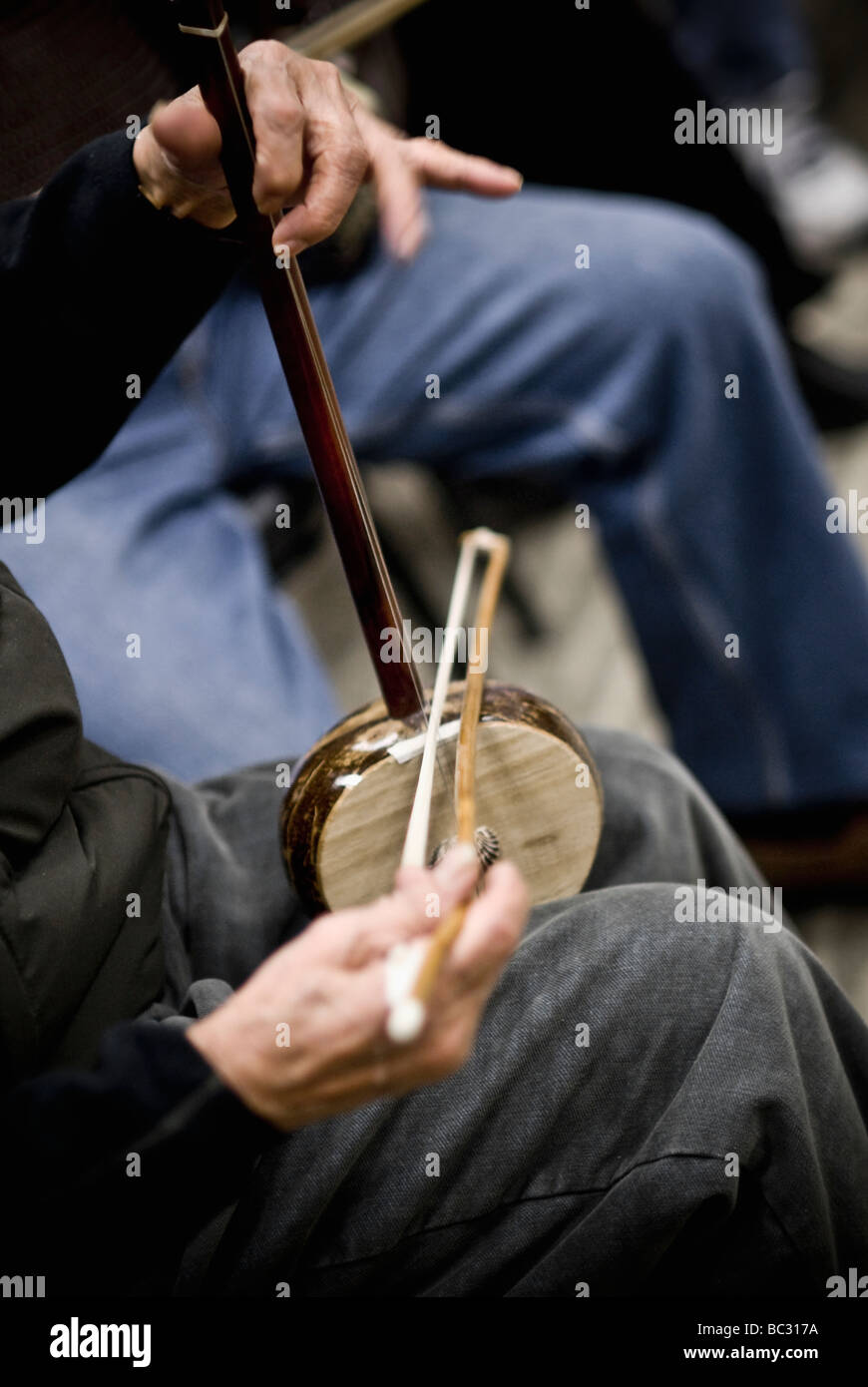An elderly man playing traditional Chinese instrument on his knees ...