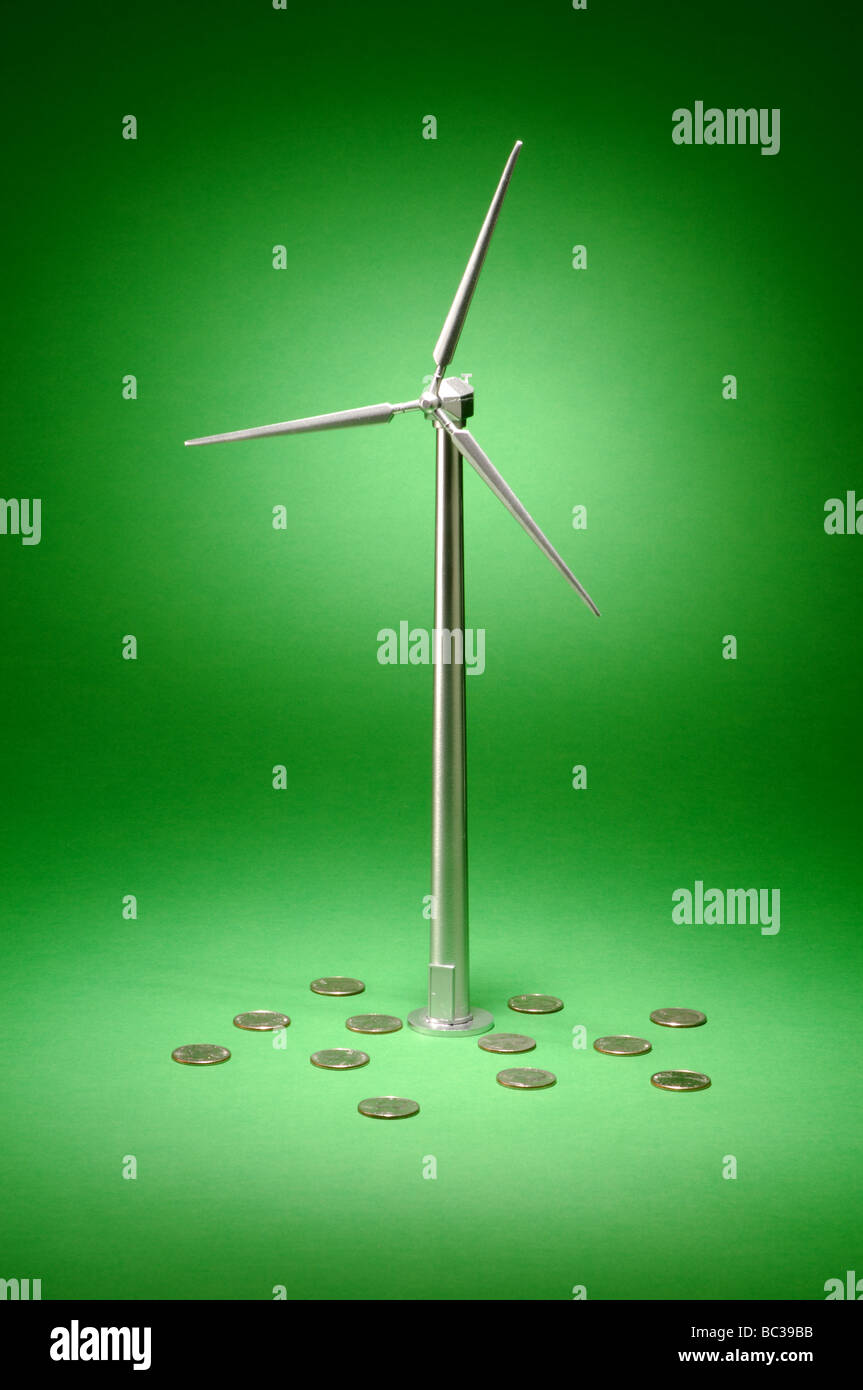A small metal wind turbine on a green background with currency coins ...