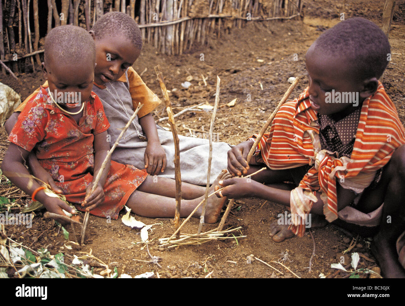Three Maasai children building traditional model house of twigs straw ...