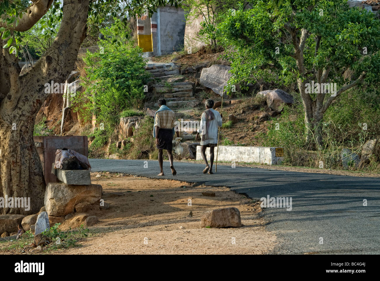 two village men one holding a chicken walking on a road past a sleeping ...