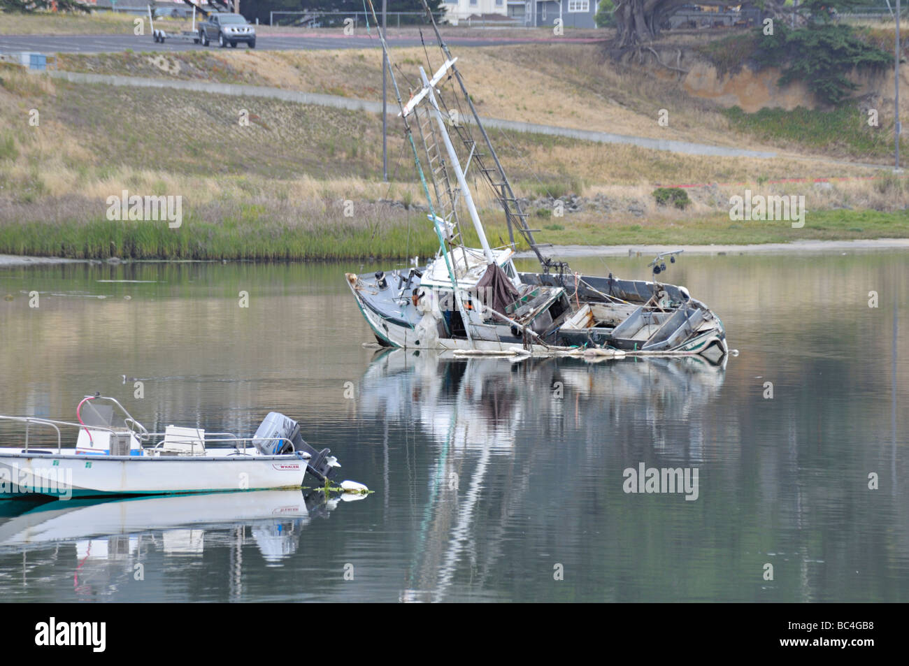 An abandoned, partially sunken fishing boat sits tilted in the calm ...