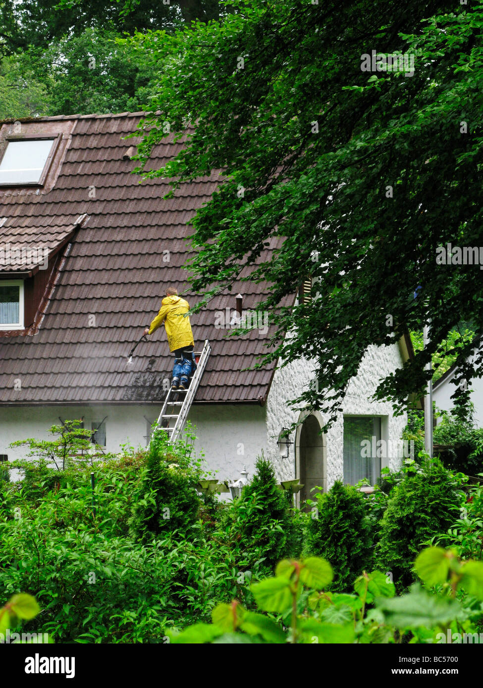 Man Wearing a Yellow Raincoat Standing on a Ladder Cleaning Roof with a ...