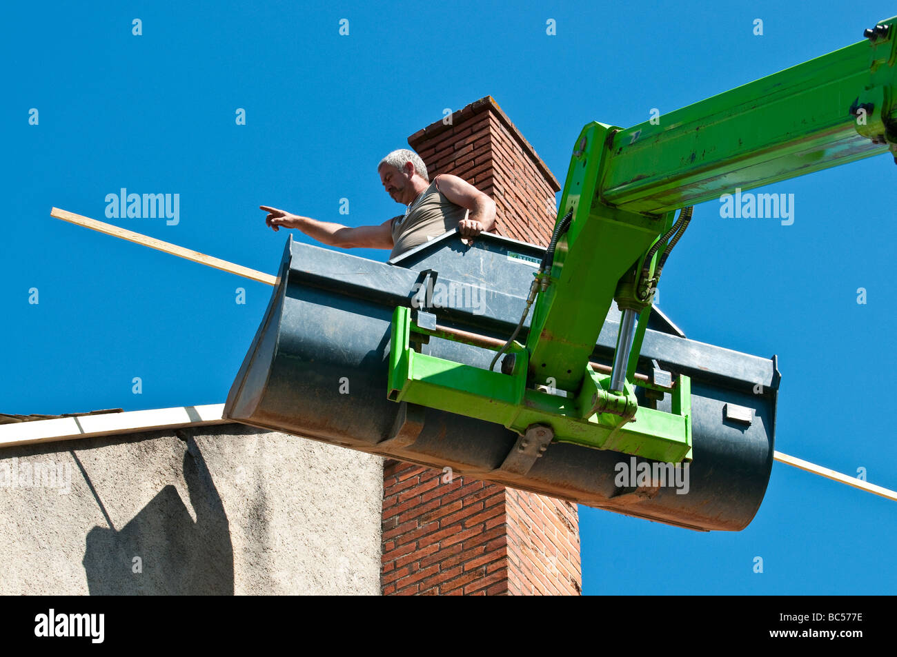 Building contractor in bucket of extending jib crane repairing house ...