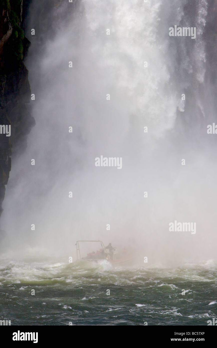 A tour boat with tourists passes under a large waterfall at Iguazu ...