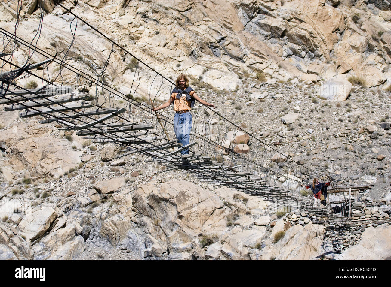 Traveller crossing a delicate rope bridge over the Hunza river ...