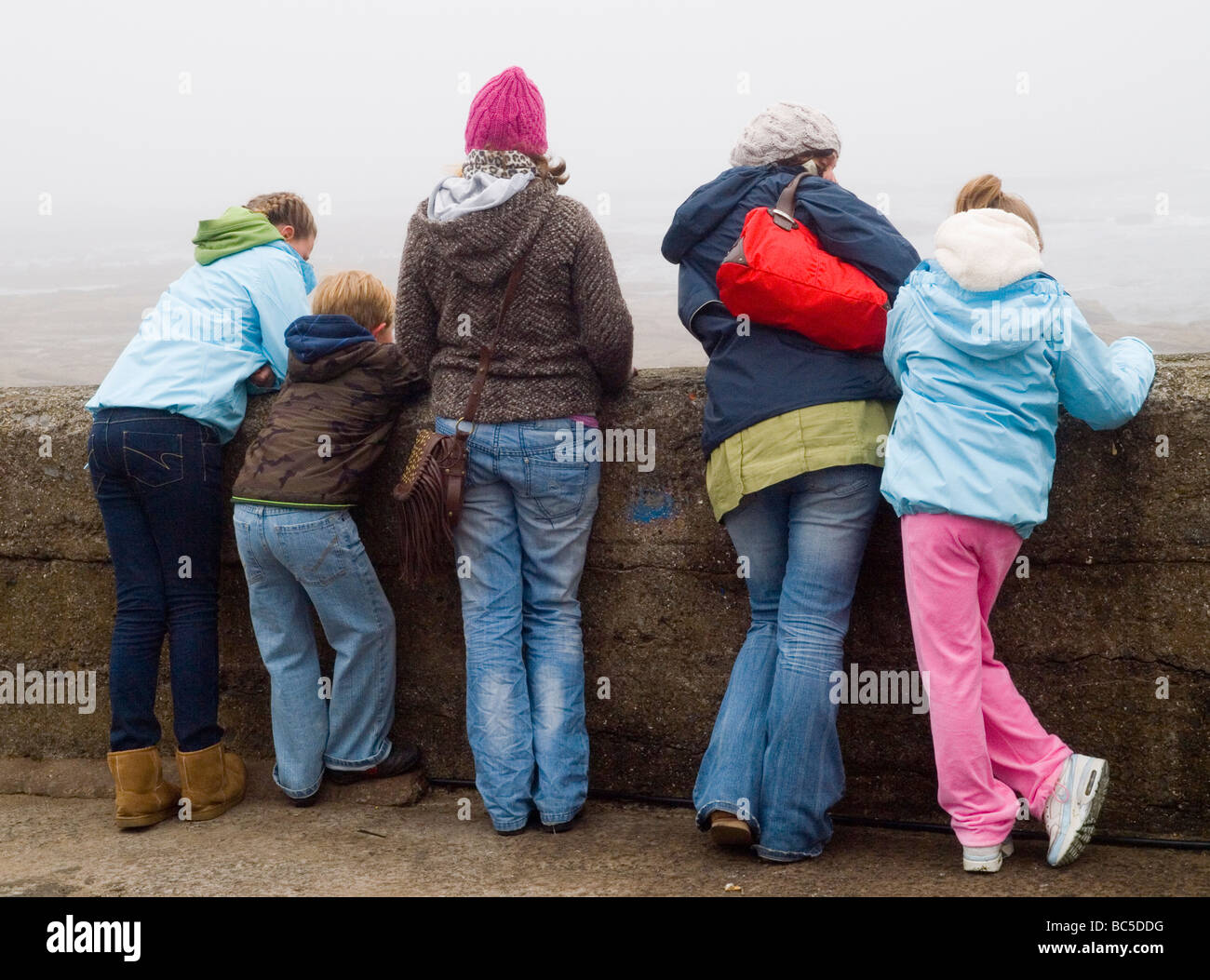 A family looking out over the seawall, on a grey overcast day in the ...