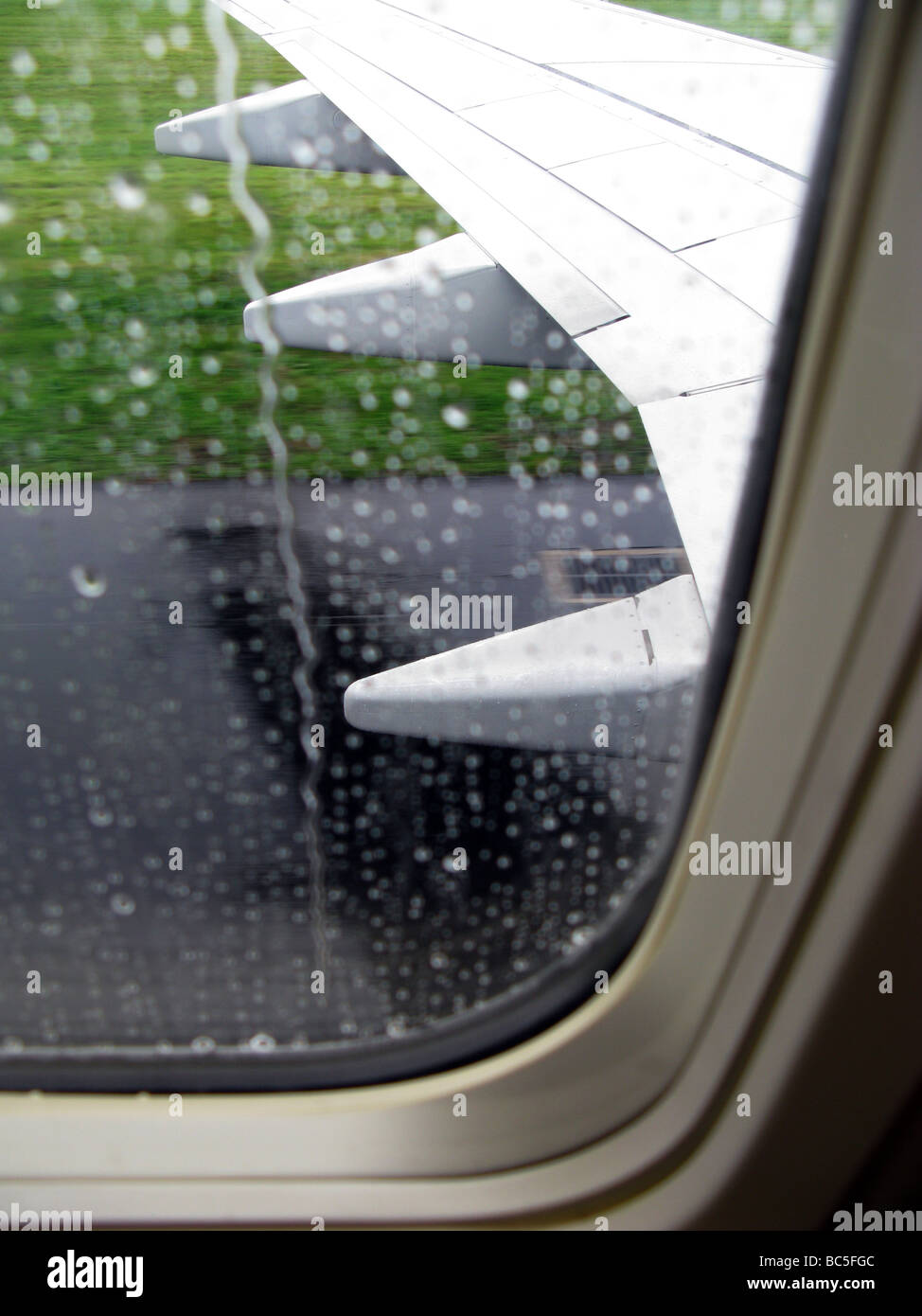 view of one wet plane wing from passenger window in rain Stock Photo ...
