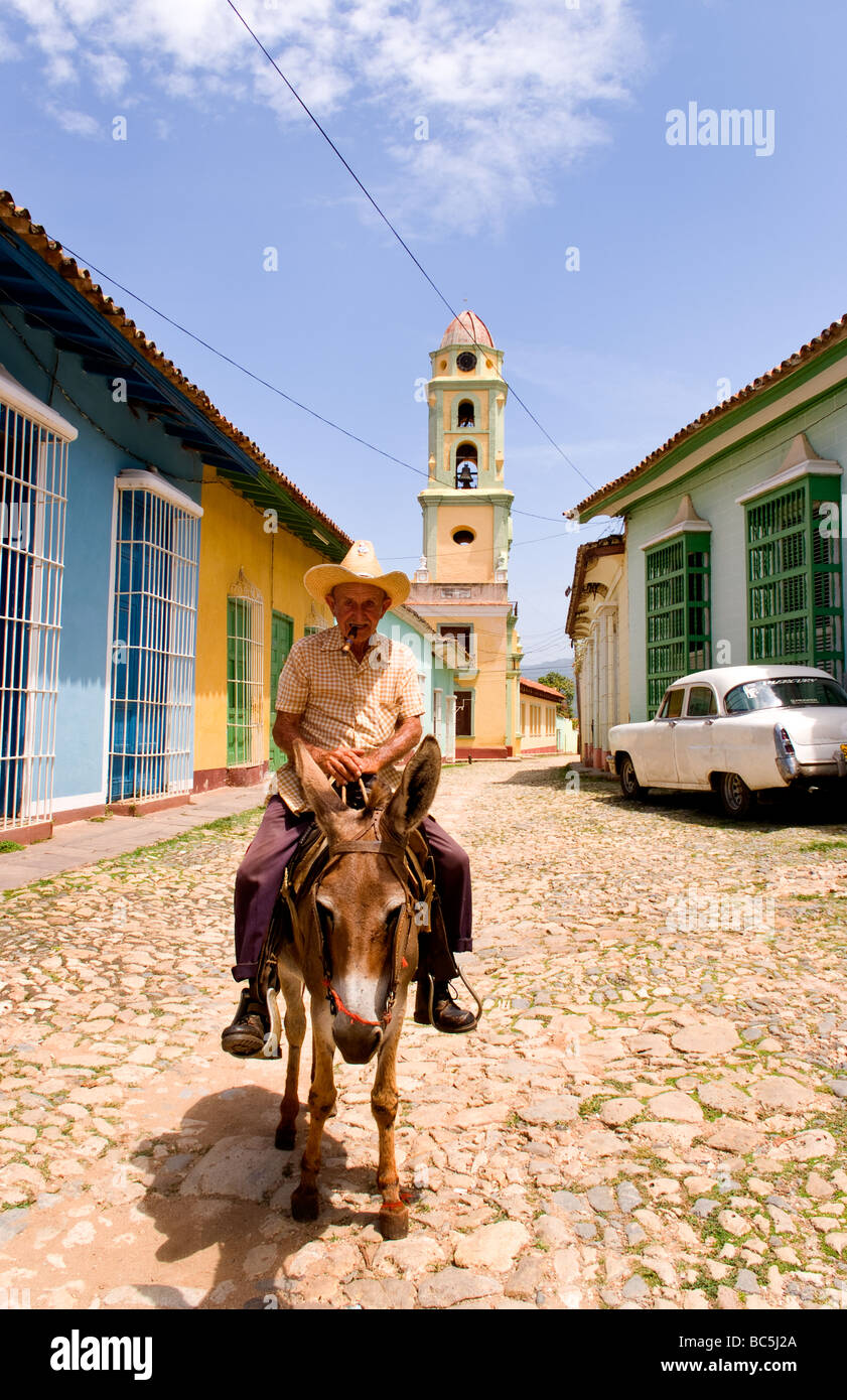 Old man riding donkey on cobblestone scene with old car in street scene ...
