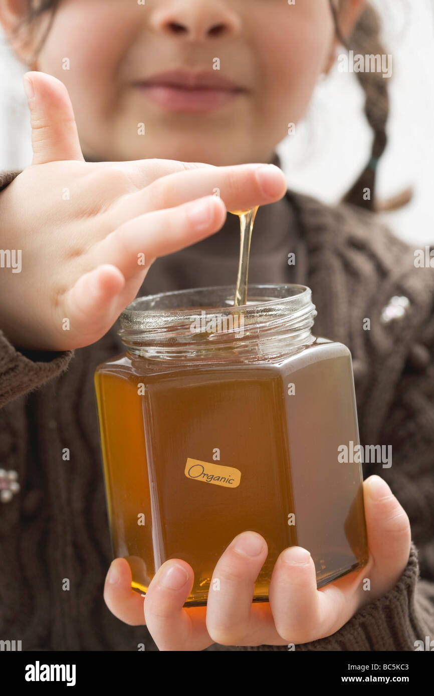 Girl dipping her finger in a jar of organic honey Stock Photo - Alamy