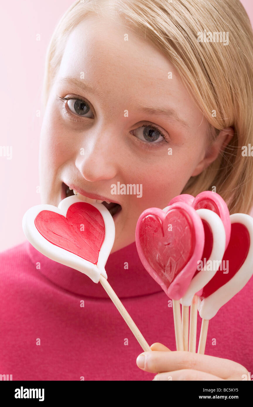 Young woman biting into a heart-shaped lollipop Stock Photo - Alamy