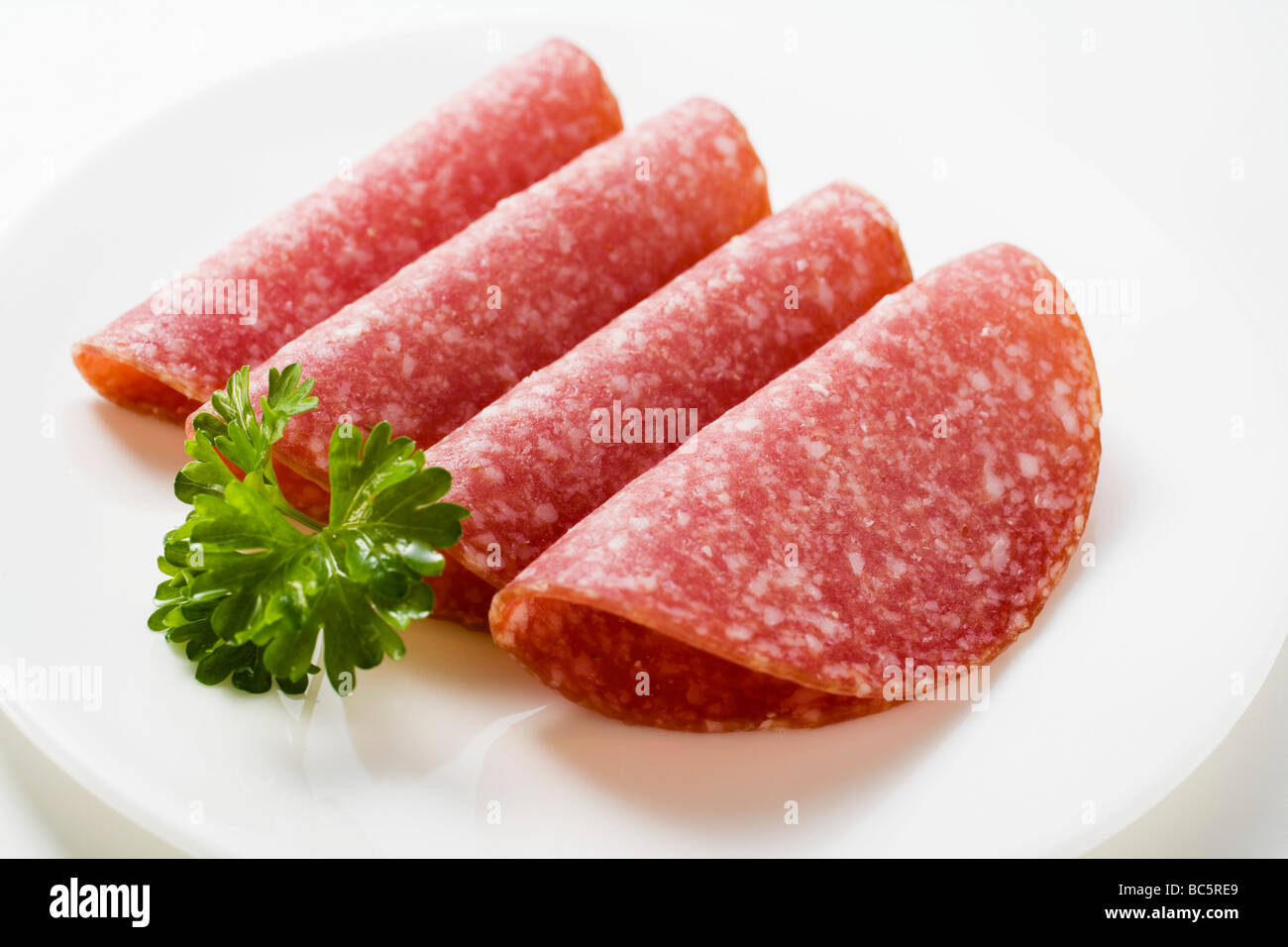 Four slices of salami with parsley Stock Photo - Alamy