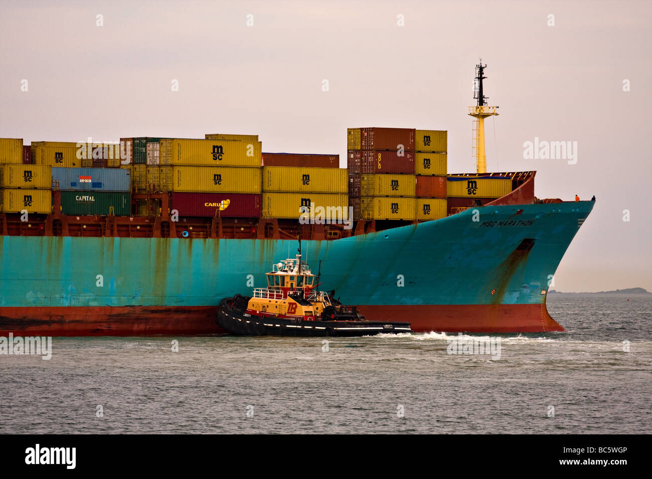 Tugboat pushing a large cargo container ship in a harbor Stock Photo ...
