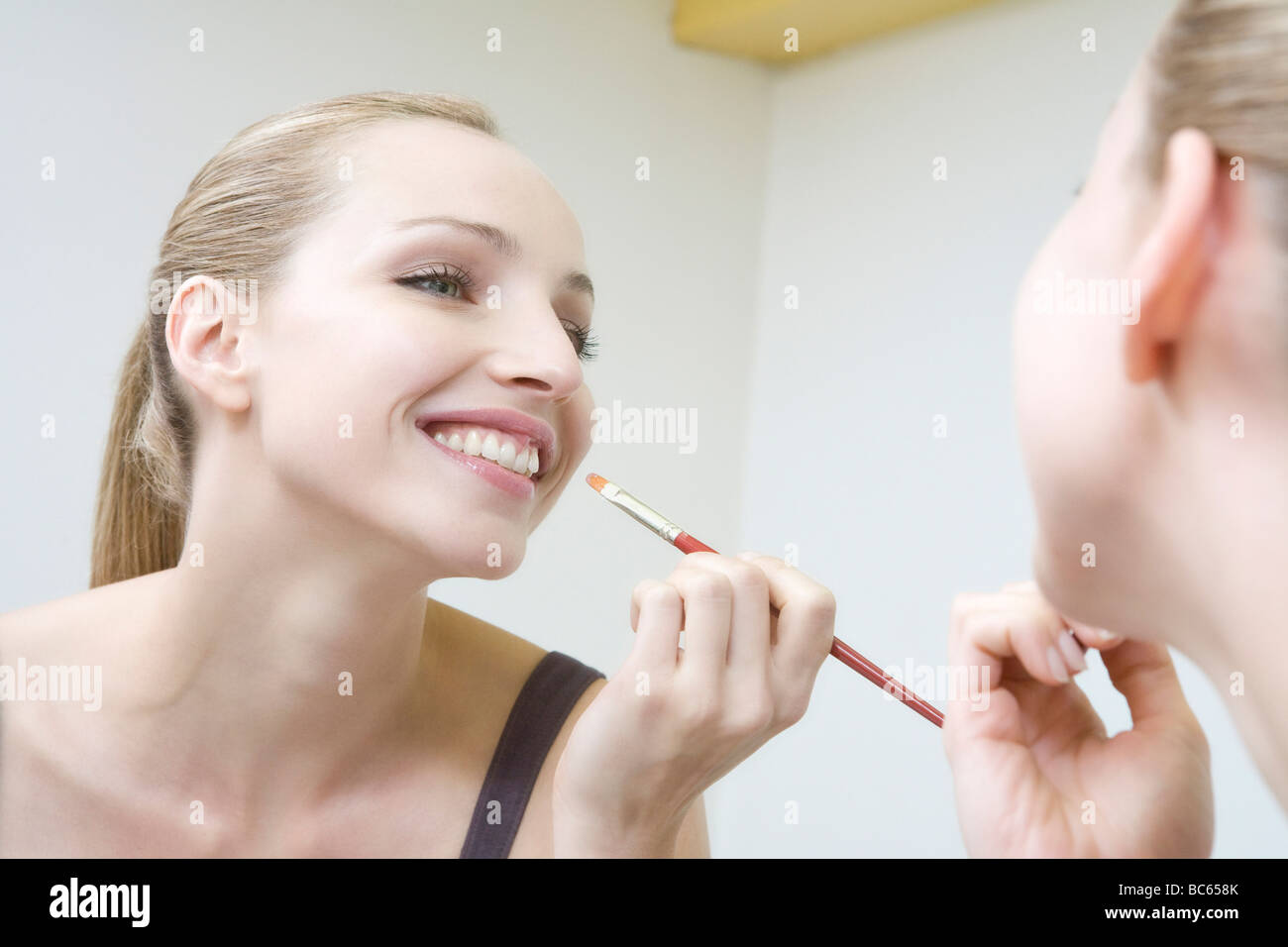 Young woman applying lipstick, smiling, portrait Stock Photo - Alamy