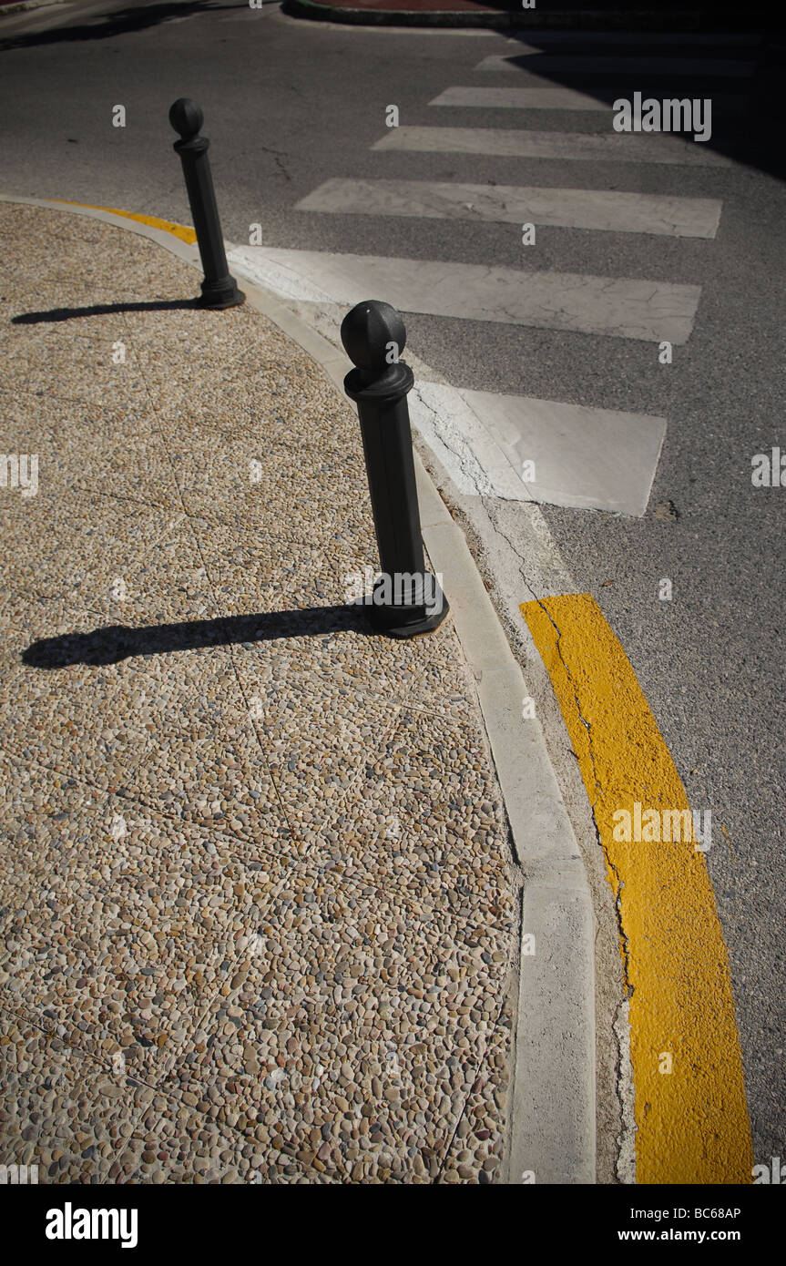Bollards cast shadows at a road crossing on a Spanish road with painted ...