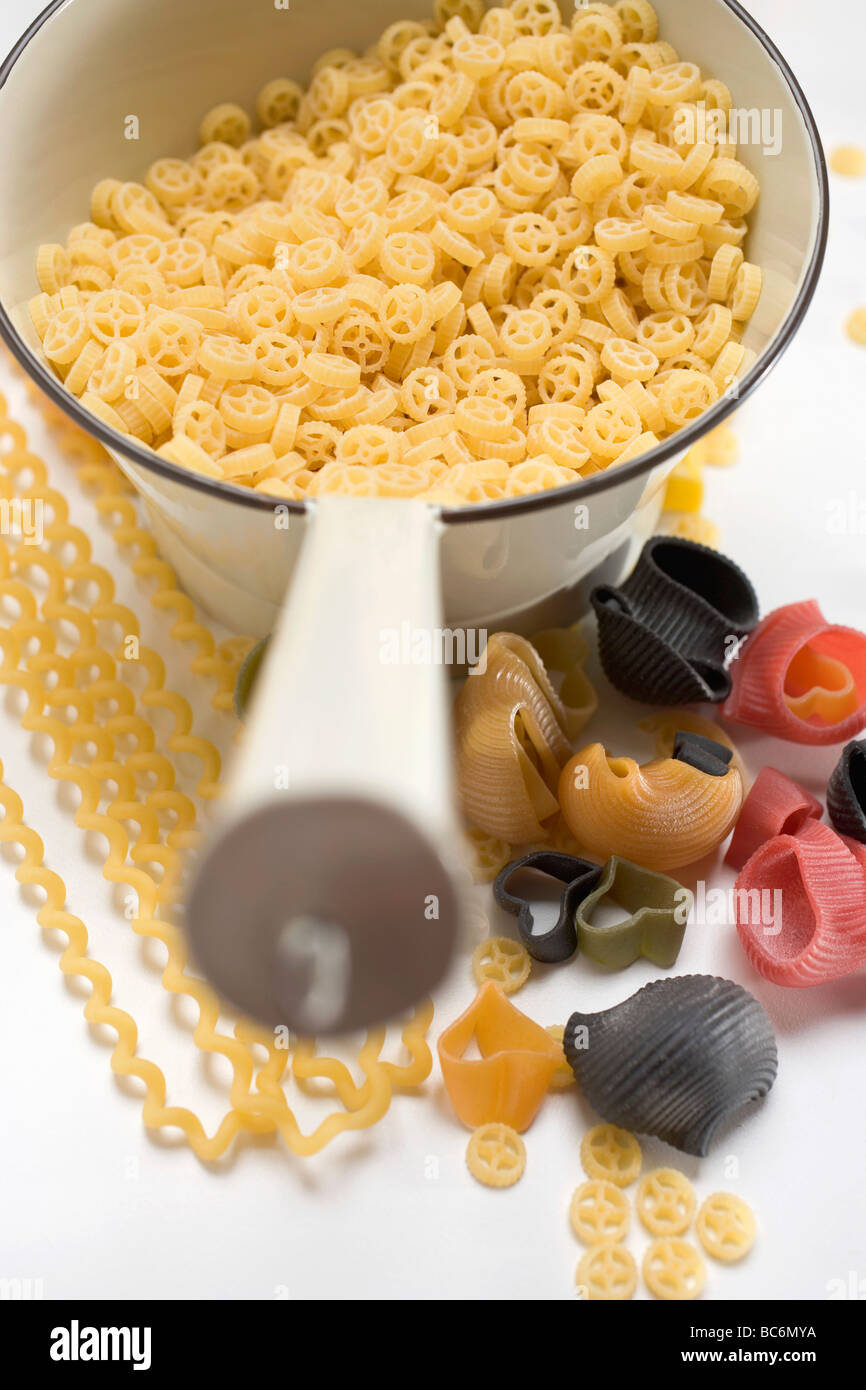 Wagon wheel pasta in strainer, coloured pasta beside it Stock Photo - Alamy