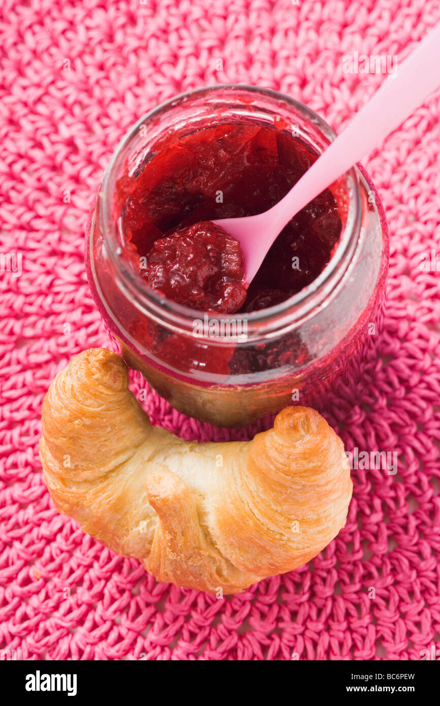 Jar of raspberry jam with spoon, croissant beside it Stock Photo - Alamy