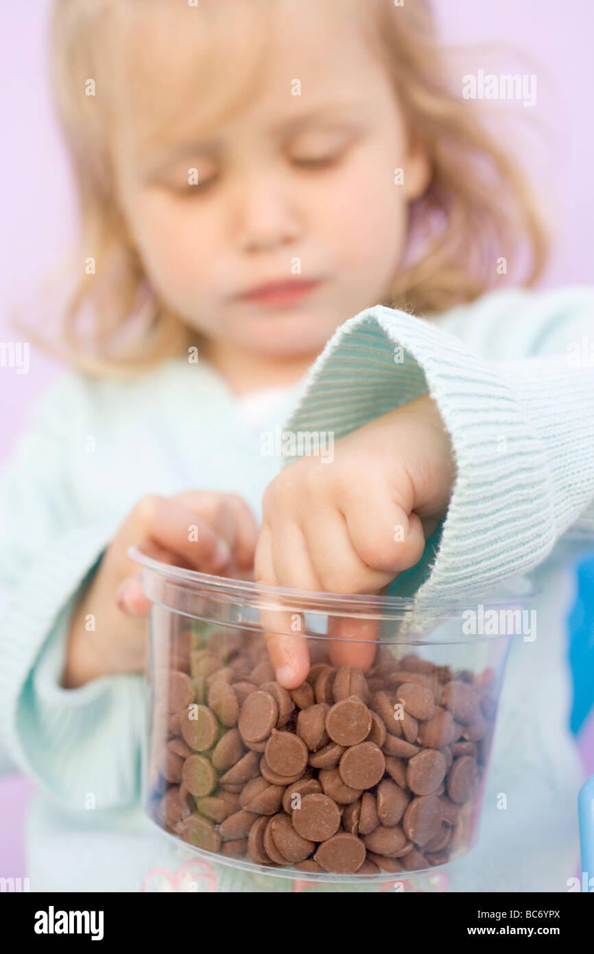 Small girl eating chocolate buttons out of plastic tub Stock Photo - Alamy